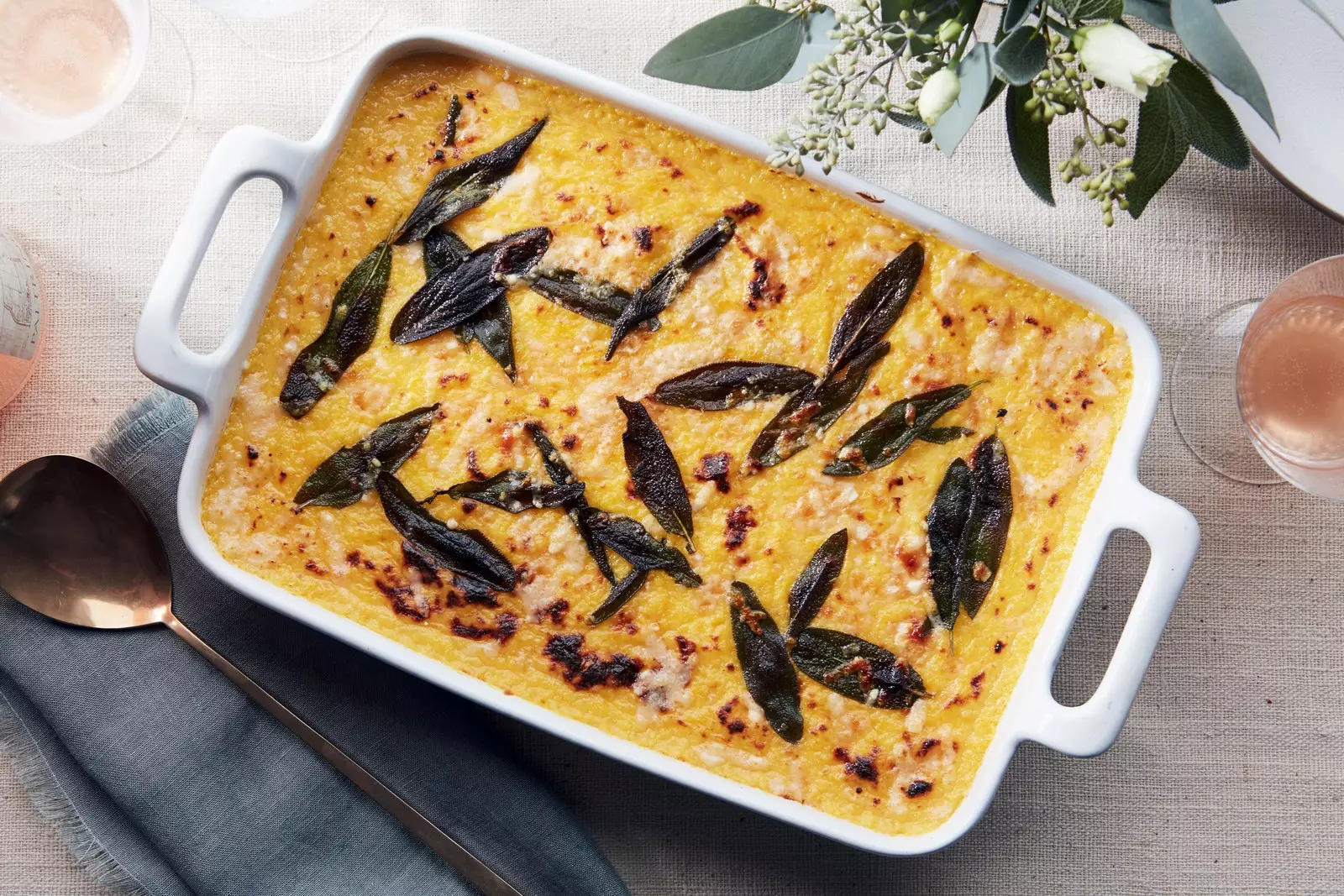 Cheesy Butternut Squash Polenta an engem wäisse véiereckege Bakform mat zwee Gedrénks an engem Portiounsläffel.