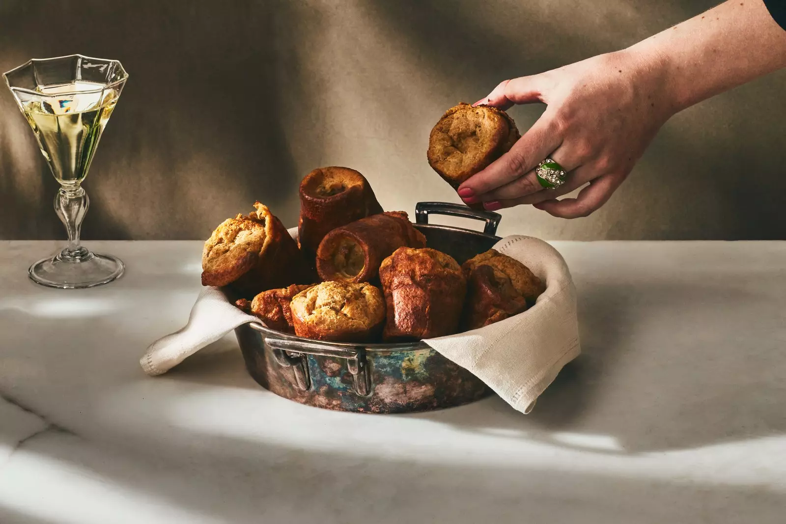 Et serveringsfat foret med en serviett og fylt med porcini popovers. En hånd som holder en popover over serveringsfatet.