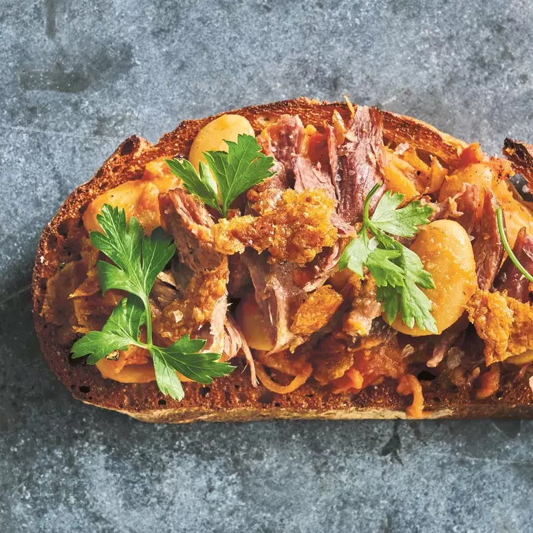 Uma única fatia de pão torrado coberto com um ragu de feijão manteiga confit desfiado e salsa.