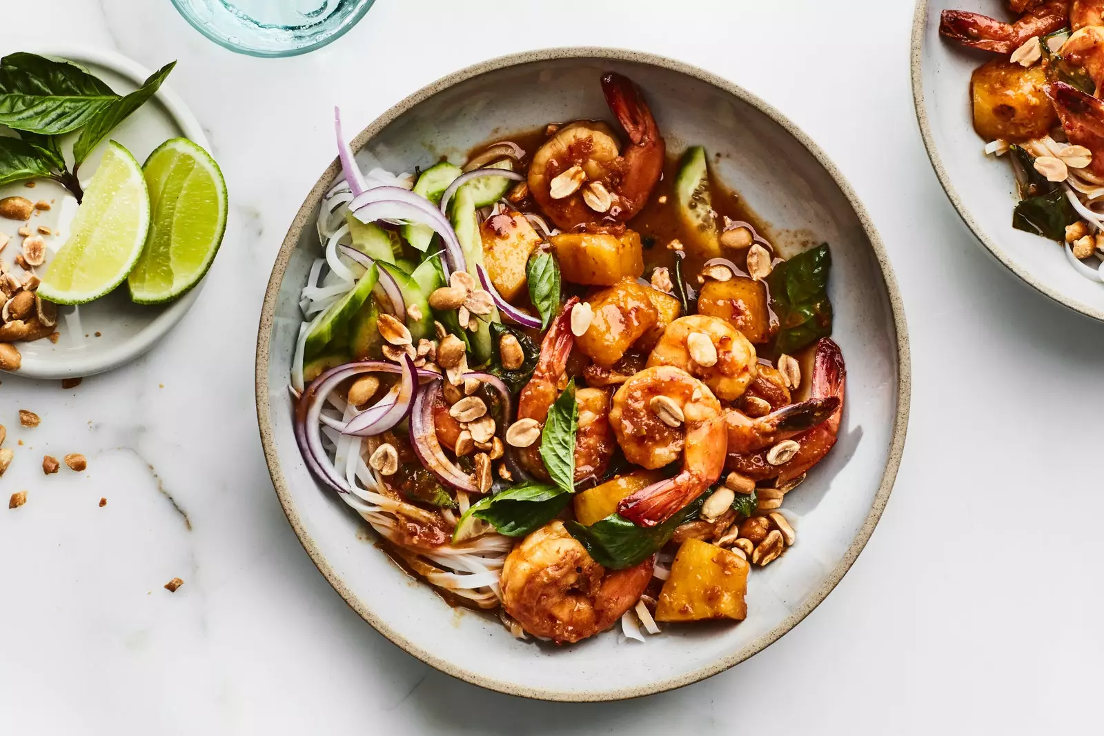 Foto von einem unserer besten Garnelenrezepte Ananasgarnelen mit Reisnudeln, Erdnüssen und Kräutern. Dargestellt mit einem Teller Limette...