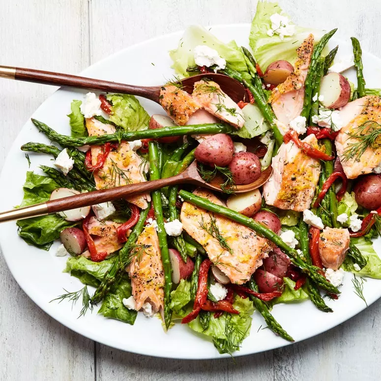 Piring saji putih di atas meja granit diisi dengan salmon asparagus dan salad escarole dengan salad kayu yang elegan. . .