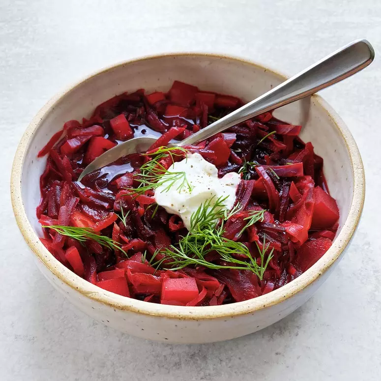 Foto af en skål borscht med en klat creme fraiche dild og en ske.