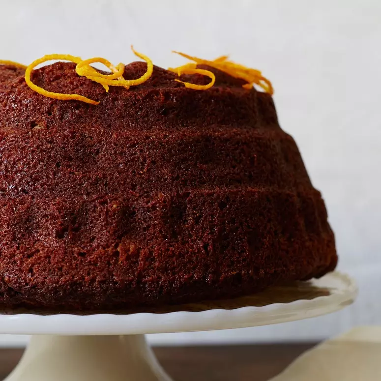 Temno rjava medena torta s pomarančnimi lupinami na belem stojalu za torte.