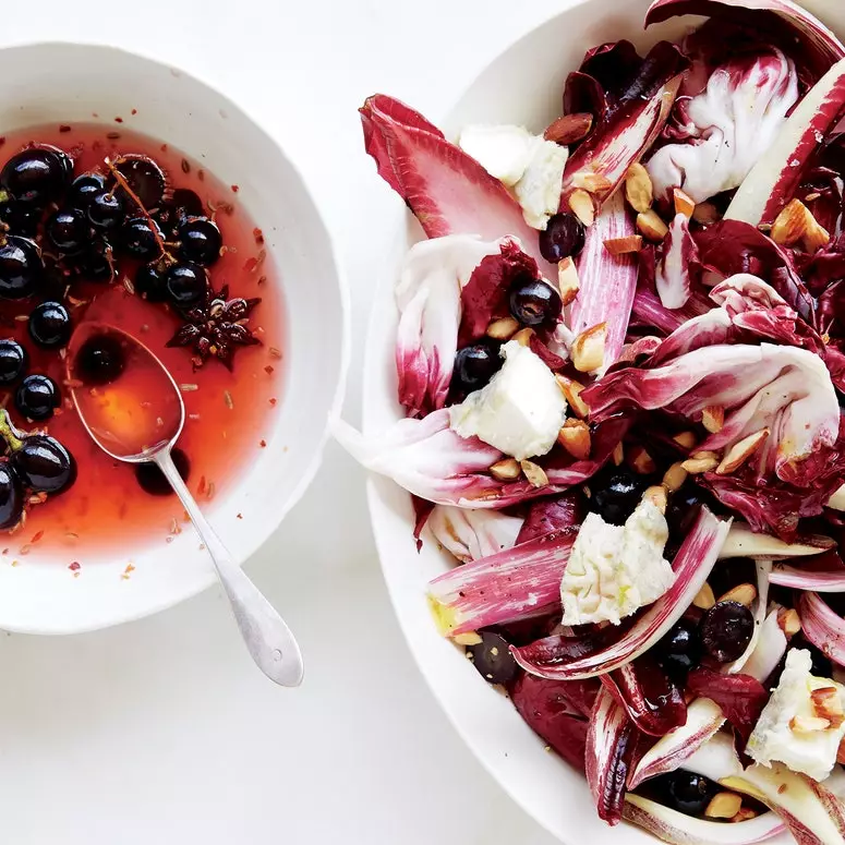 Isang hugis-itlog na ulam na may radicchio salad. Sa kaliwa ay isang mangkok ng adobo na ubas na may isang kutsara sa loob nito.