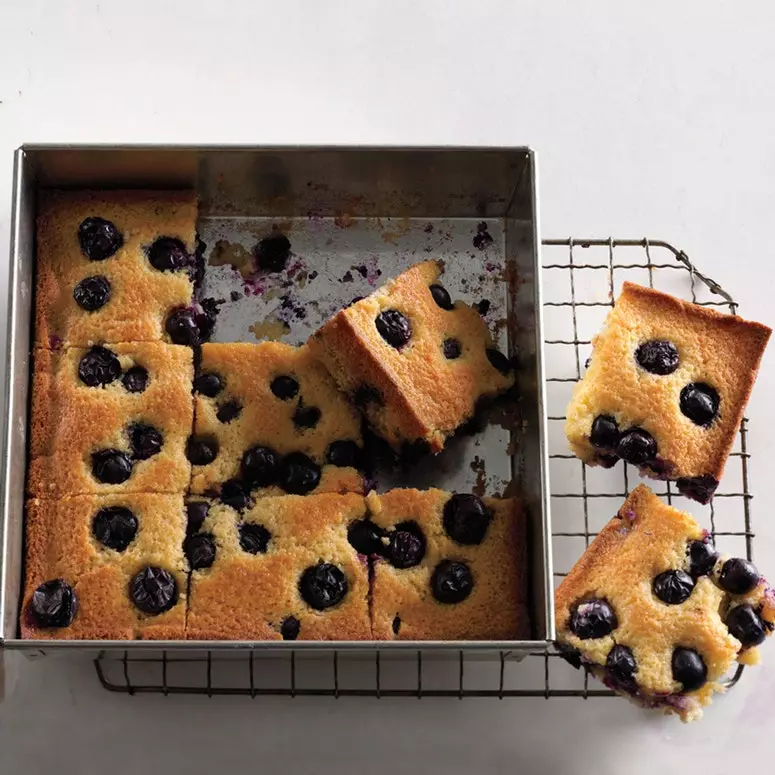 Concord grape cornmeal cake sa isang parisukat na baking dish na may dalawang hiwa sa gilid sa isang cooling rack.