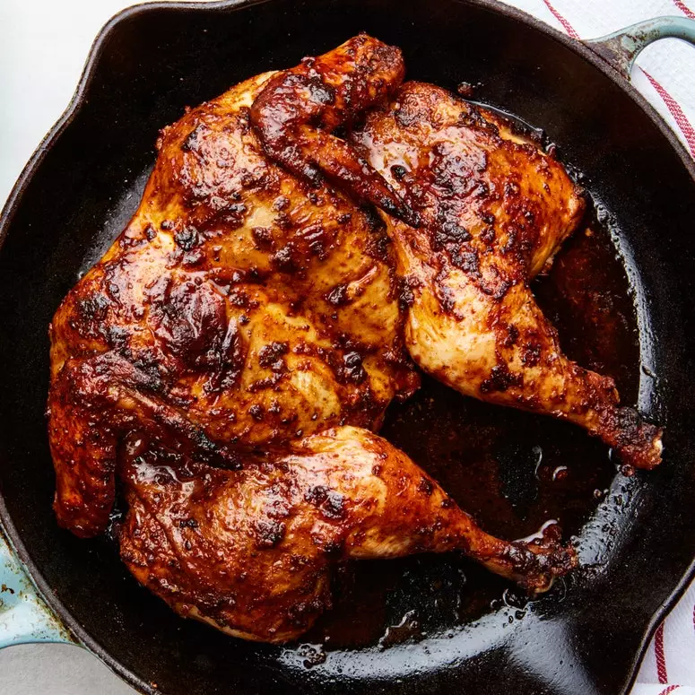 Снимка на любимата ни перуанска рецепта за печено пиле, показваща пилето в чугунен тиган с малък съд с...