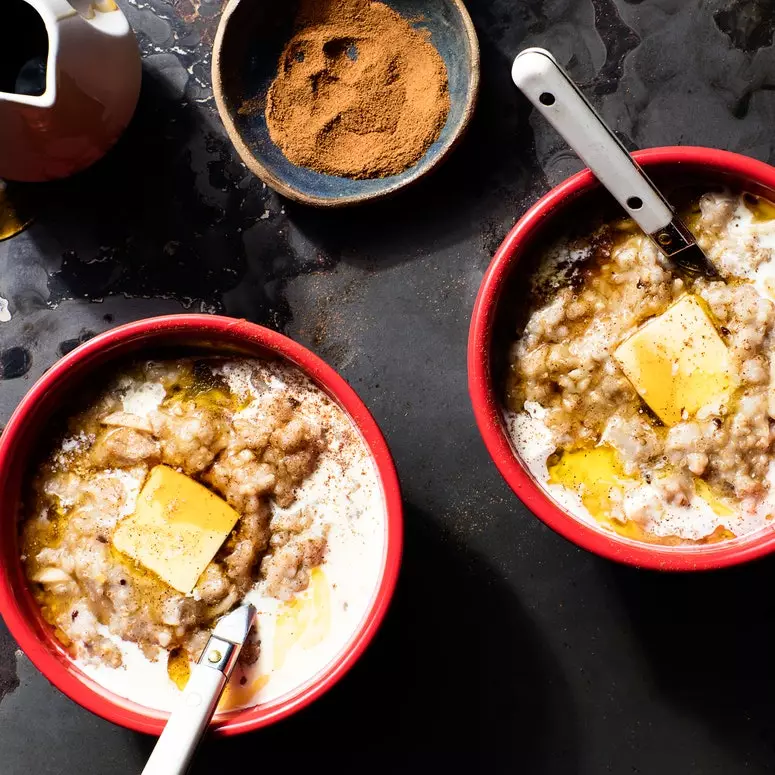 Dúas cuncas de avea cubertas con crema de manteiga derretida e canela e un chorriño de xarope de bordo.