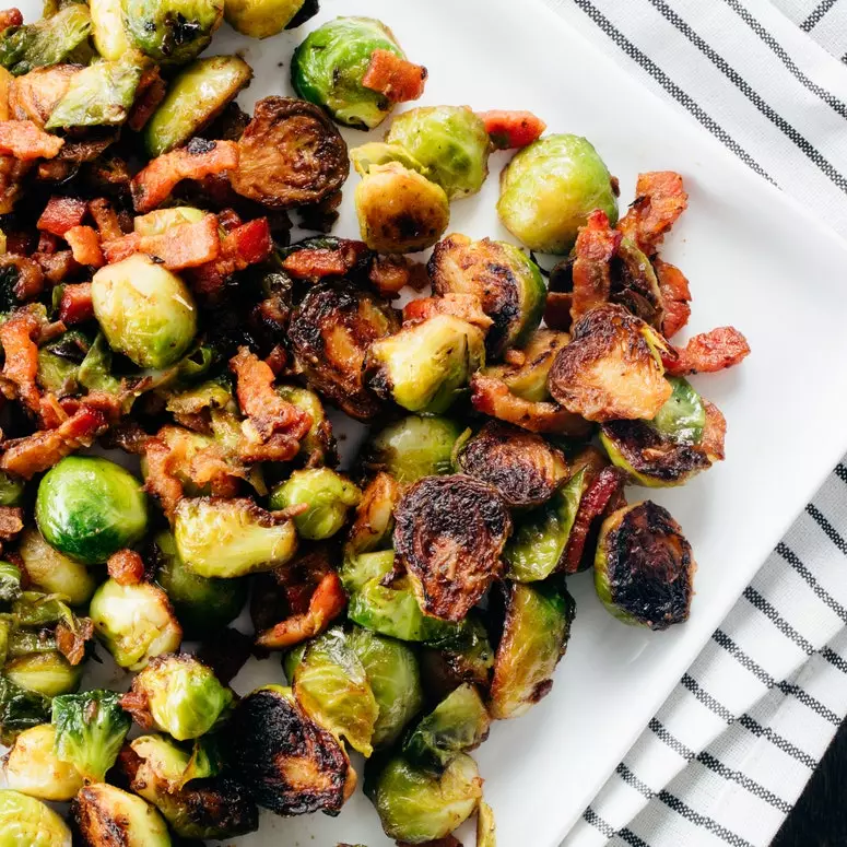 Panroasted Brussels huchipua na Bacon kwenye sahani nyeupe ya kuhudumia.