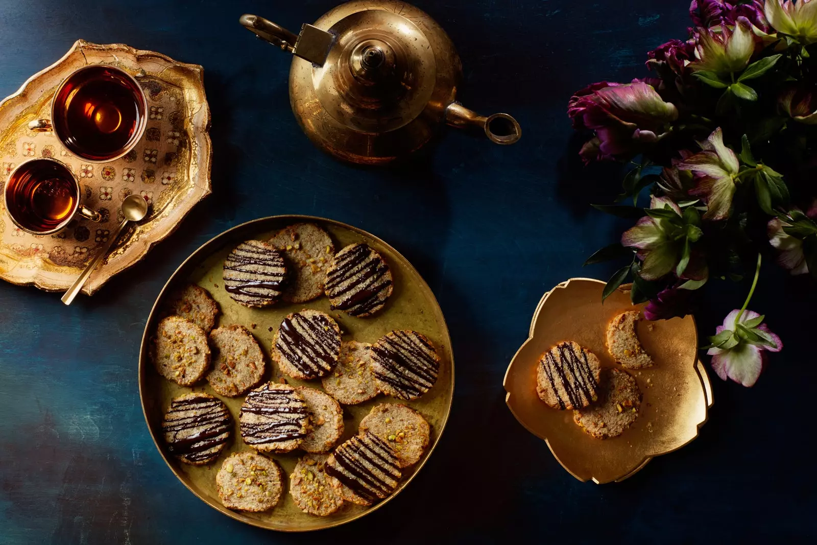 Almond cookies nga adunay cardamom orange zest ug pistachios sa bulawan nga mga platter batok sa itom nga background.