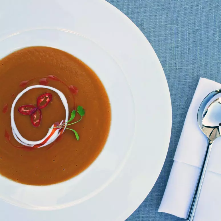 Поглед одозго на веганску супу од слатког кромпира и кокоса у белој посуди са украсом од уља од чилија.