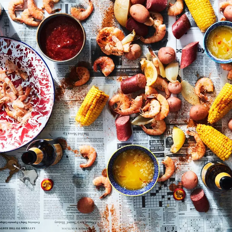 LowCountry Boil Ferspraat garnalen maisworstjes en ierappels op in krantebedekte tafel.