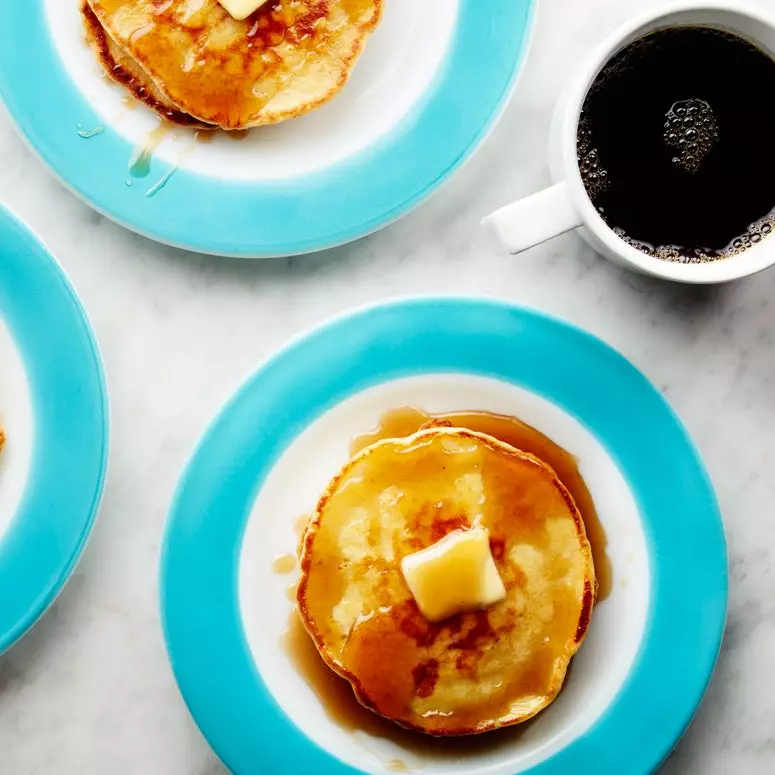 Pancake dengan sapuan mentega dan sirap maple di atas pinggan berbingkai biru.