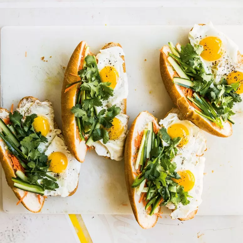 Empat baguette mini dibelah dan disumbat dengan dua telur goreng setiap sayur jeruk dan ketumbar.
