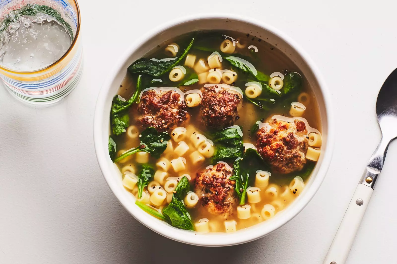 Frikadellesuppe med grønt og pasta i hvid skål.