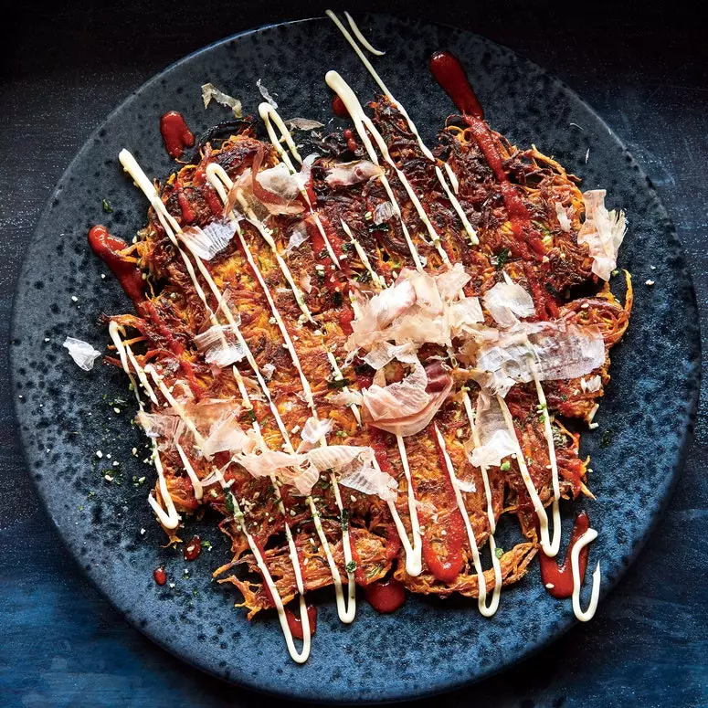 Une fine crêpe de patates douces râpées sur une assiette avec des gribouillis dramatiques de mayonnaise et de Sriracha.