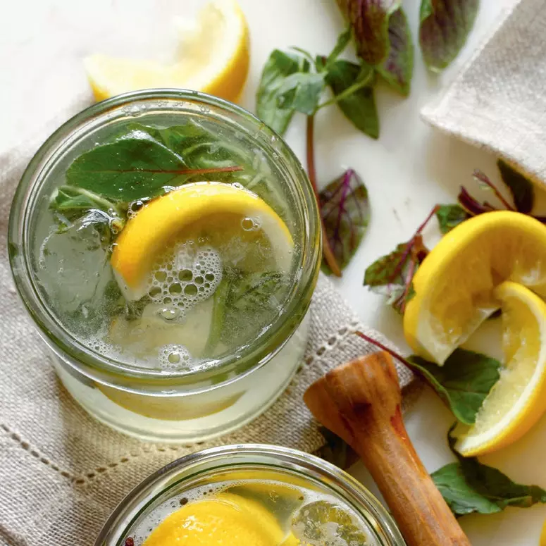 Cocktail di gin con basilico e limone in tre tumbler di vetro con muddler e spicchi di limone.