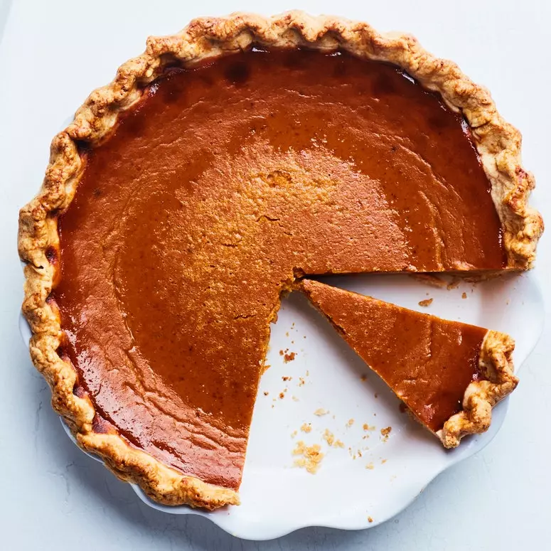 Bêste Pumpkin Pie Recipes foar Thanksgiving 2021. Bourbon pumpkin pie mei ferskate plakjes nommen út it taart skûtel.