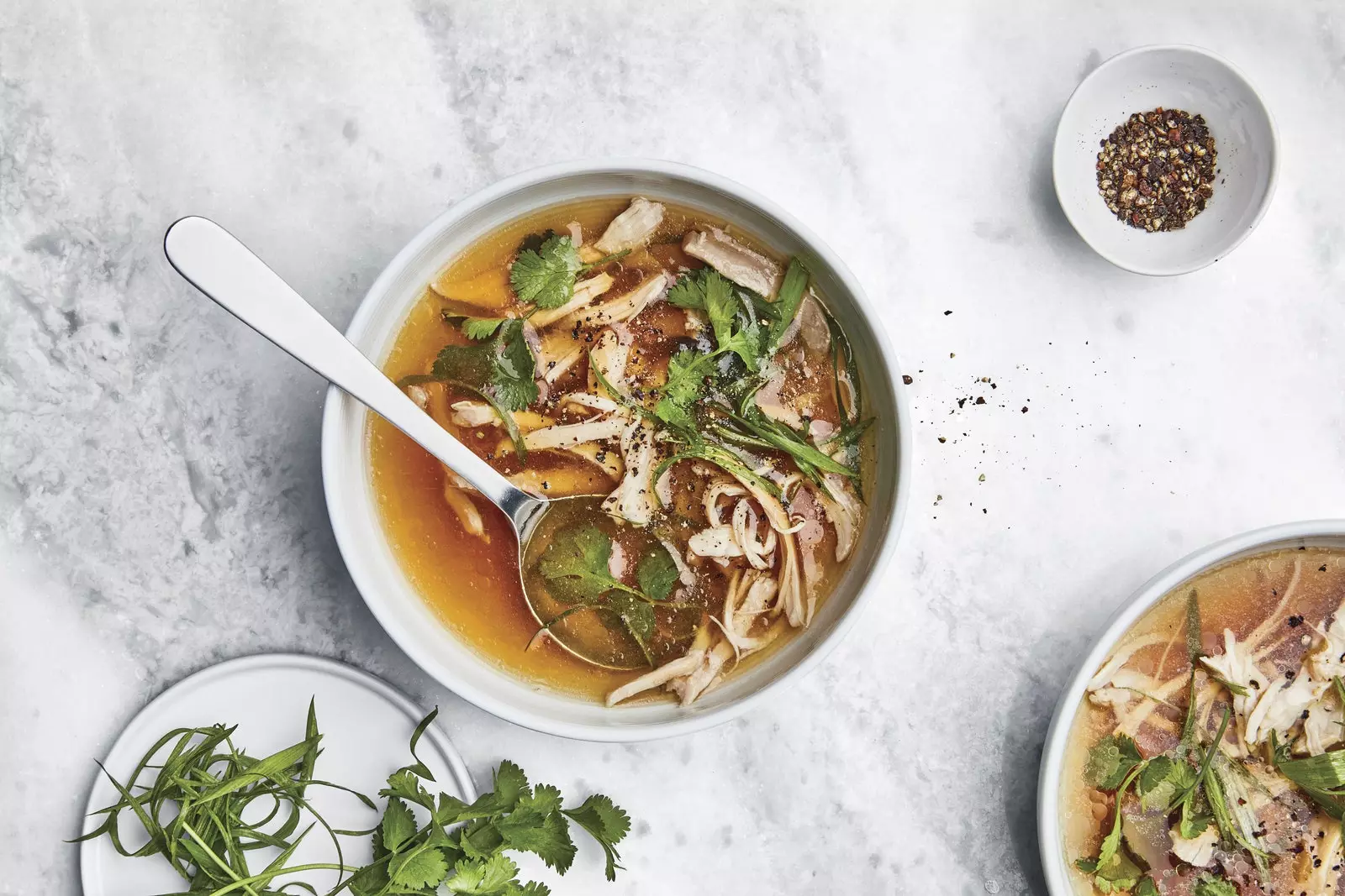 Un bol de sopa de pollastre sobre una superfície de marbre amb un brou profundament bronzejat amb grans trossos de pollastre i guarnit amb coriandre.