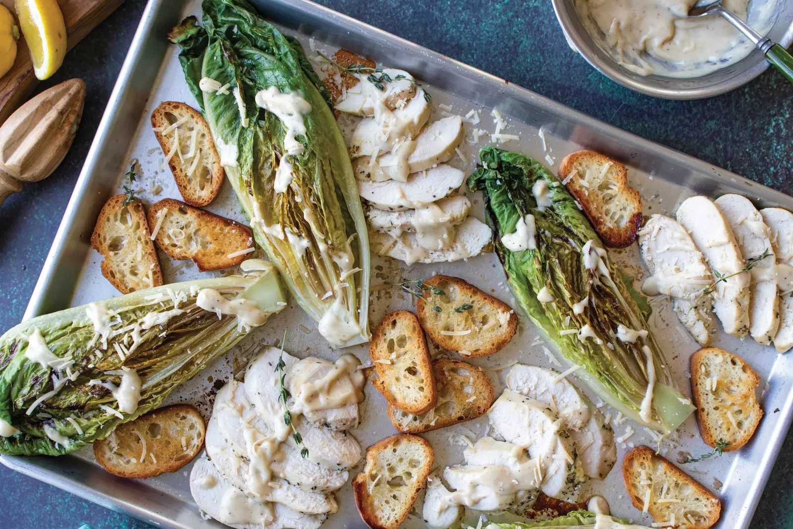 En una bandeja de hojas, rebanadas de pechuga de pollo asadas, rociadas con aderezo César, corazones de crostini de lechuga romana carbonizados y partidos por la mitad.