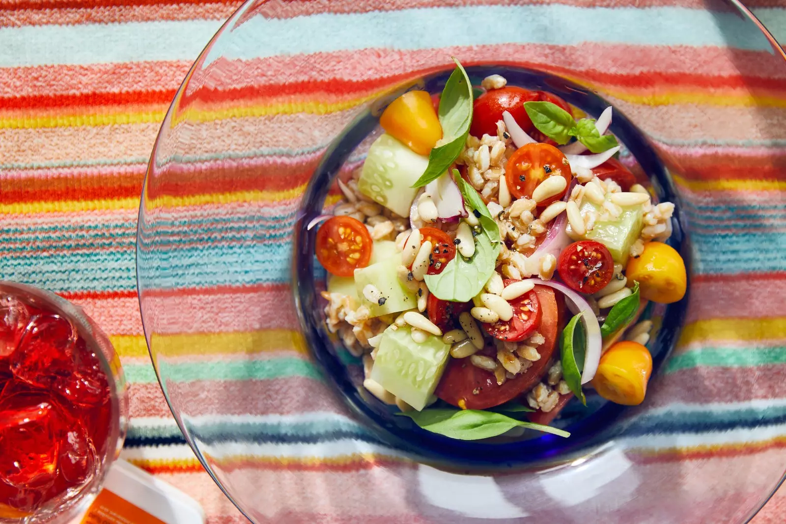 Foto di un'insalata di cereali con pomodori e cetrioli in un piatto di vetro su un panno a righe.
