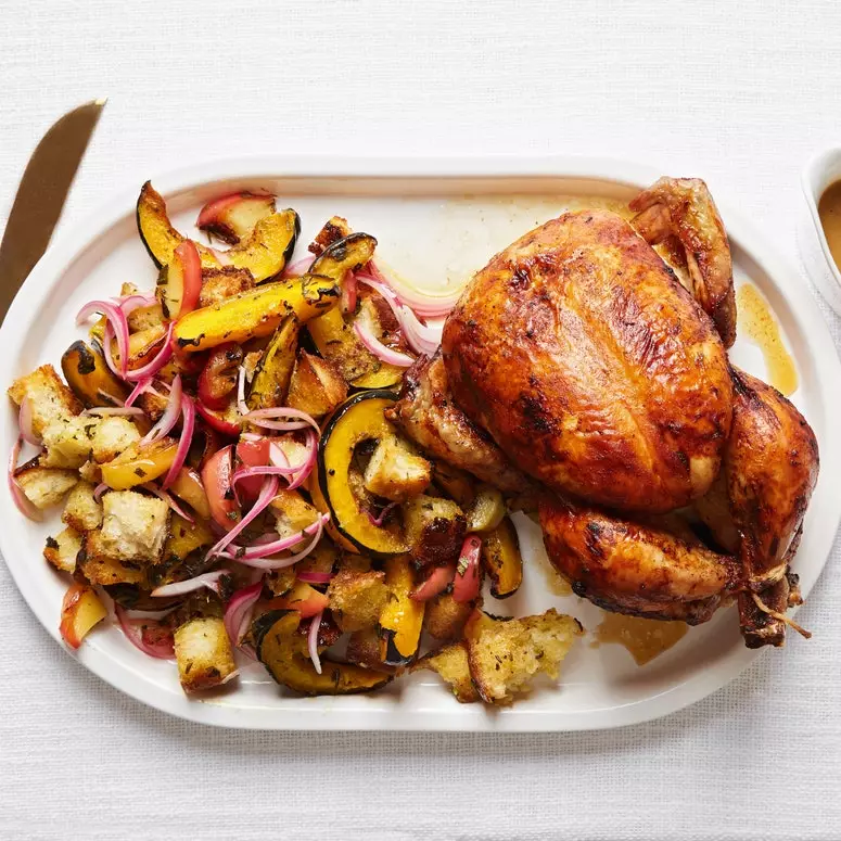 一张烤鸡在盘子上的照片，上面有胡桃南瓜、一碗肉汁和旁边的餐具。