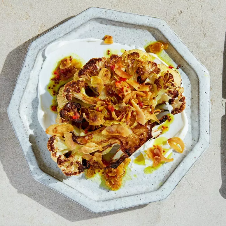 一个白盘子，上面有花椰菜牛排和椰子姜黄酱。盘子左边是叉子，右边是叉子……