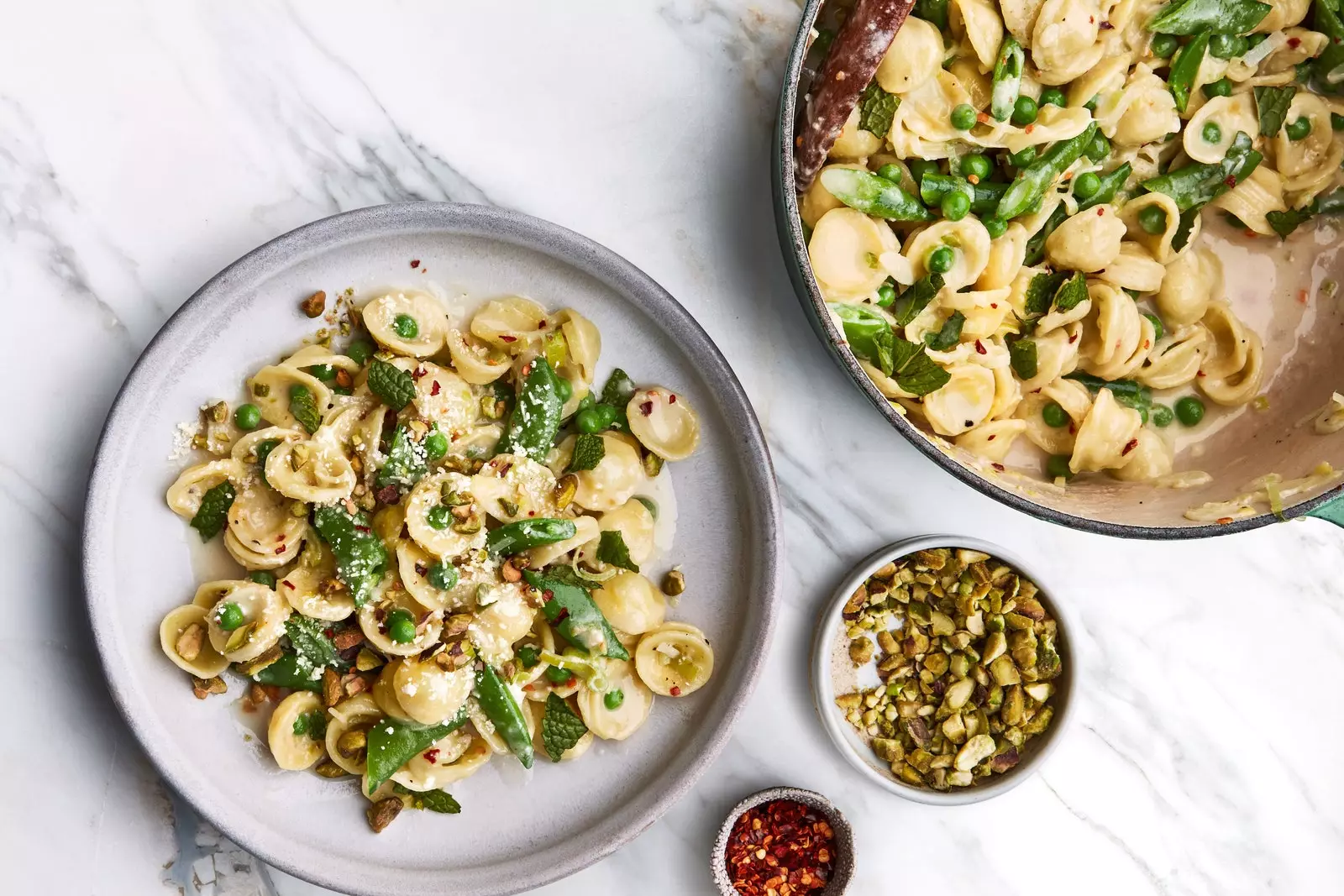 Prato de pasta xunto a un forno holandés con máis do mesmo e un pequeno prato de pistachos picados.