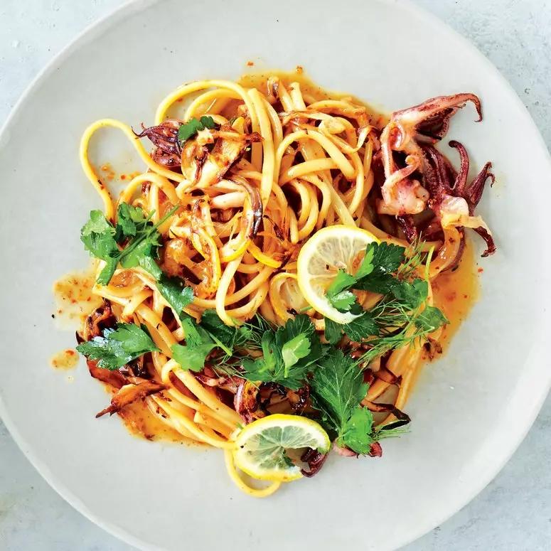 Nouilles spaghetti mélangées à des tentacules de calmar et parsemées de tranches de citron et de menthe grossièrement hachée.