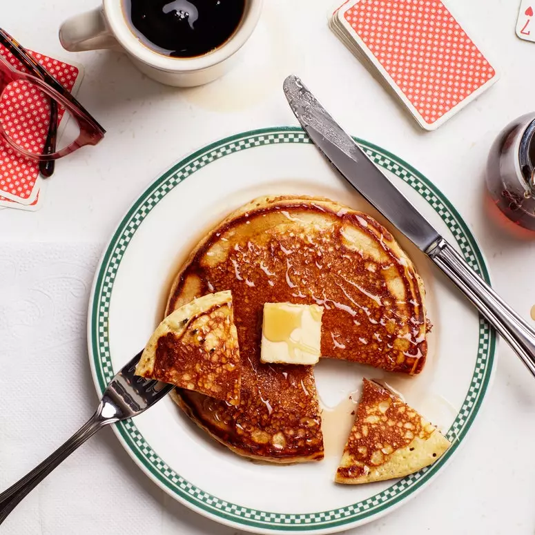 Larawan ng pancake sa isang plato na may tinidor na kutsilyo at maple syrup.