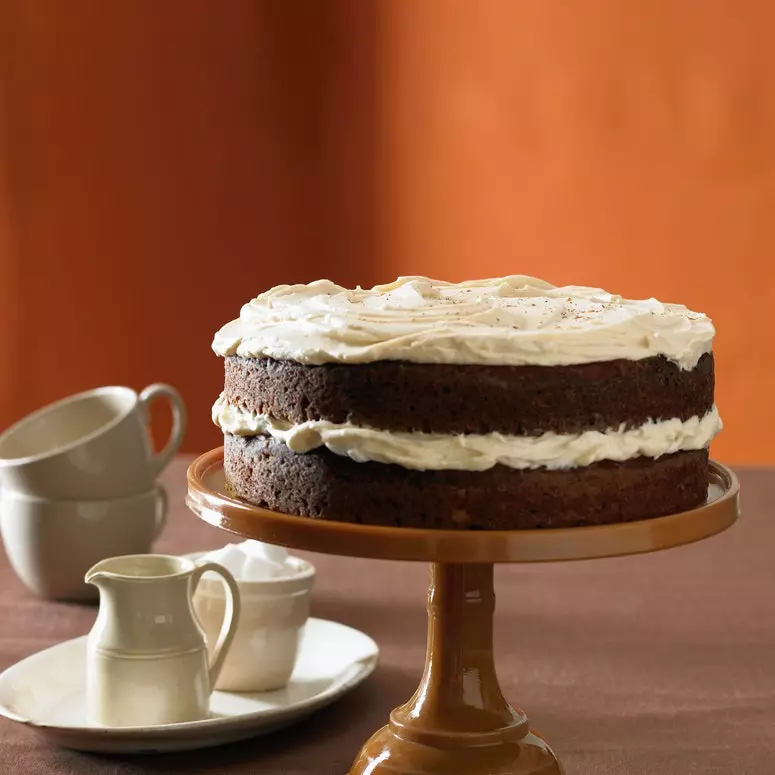 Пряный тыквенный слоеный пирог с глазурью из сливочного сыра на коричневой подставке для торта.