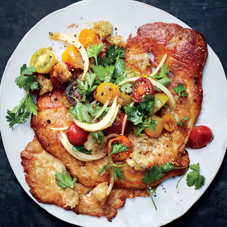 Foto que muestra la receta de chuletas de pollo crujiente de Alison Roman en un plato con tomates cherry y hierbas.