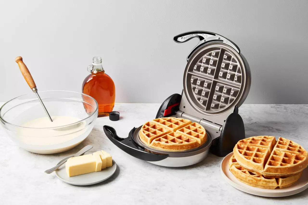 Wêneyê Waffle Makerê Presto li ser rûpek mermerî bi waffles, batter, rûn, û syrupa nêriyê Belçîkî.