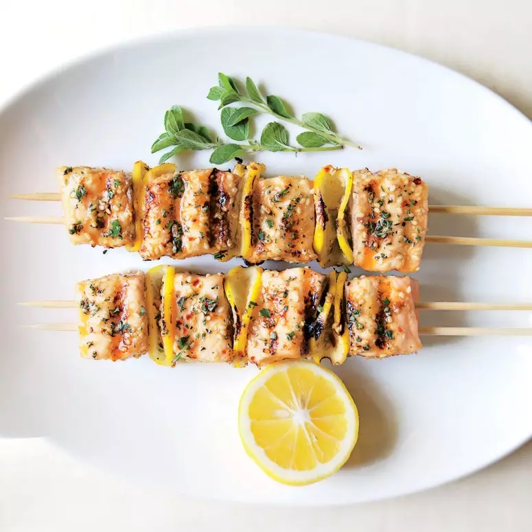 Salmon kebabs abụọ na skewers osisi na efere nwere ọkara lemon maka sqeezing.