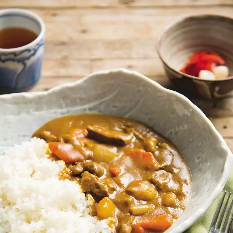 Zdjela japanskog curryja i bijele riže s priborom za jelo i zelenim ubrusom.