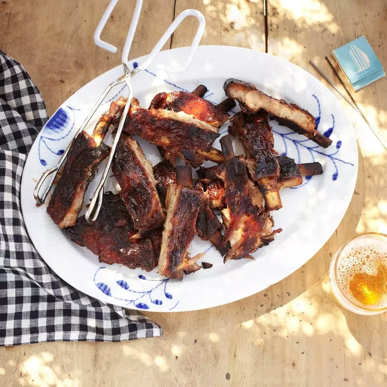 Poto iga babi barbecue nu geus dipanggang grilled tur disusun dina platter kalawan porsi tongs.