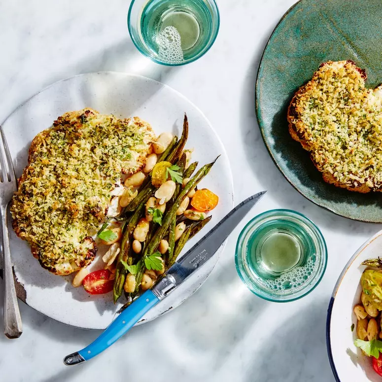 Steaks de chou-fleur en croûte d'herbes avec haricots blancs, haricots verts et tomates.