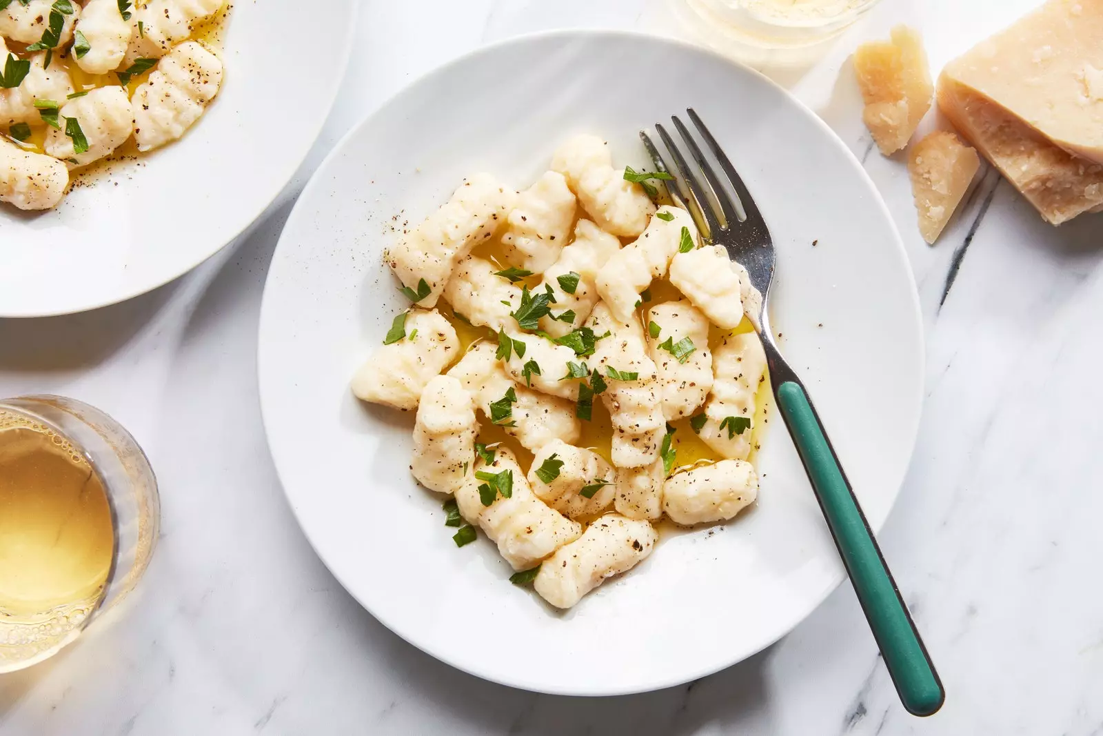 Grianghraf de gnocchi déanta le calóga prátaí seirbheáilte le im leáite agus peirsil mionghearrtha.