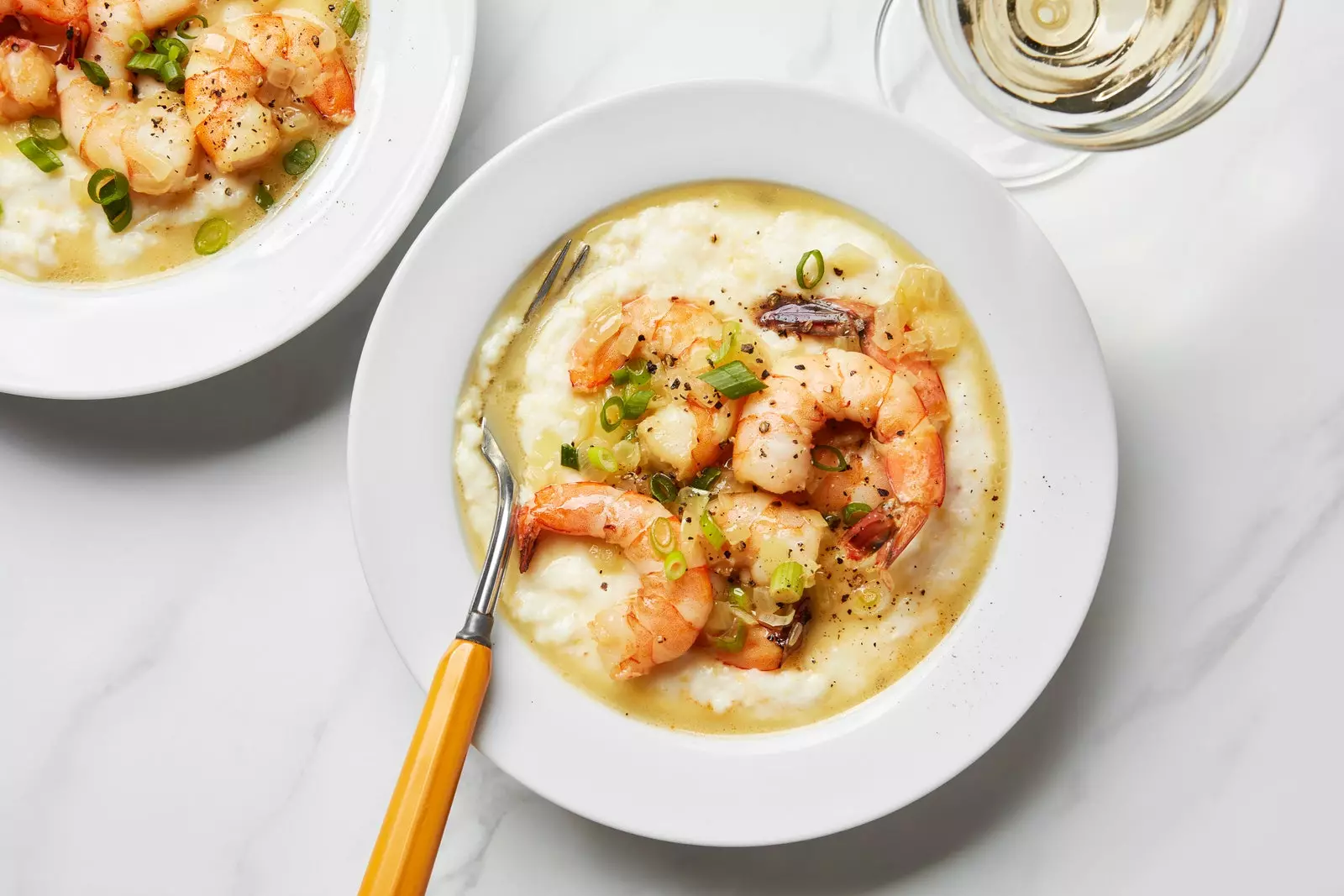 Dvije zdjele Lowcountry Breakfast Shrimp sa čašom bijelog vina sa strane.