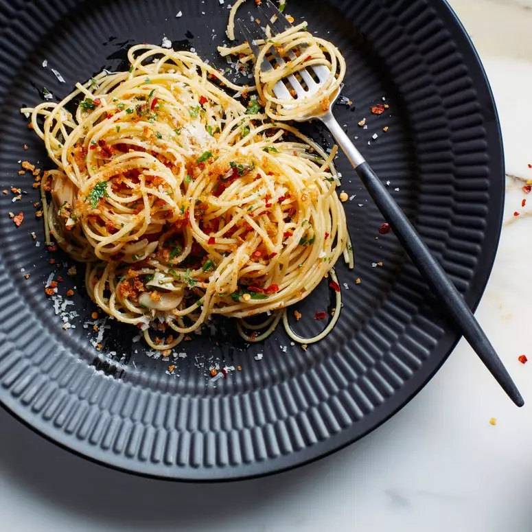 Vienkāršas makaronu receptes, piemēram, ķiploku un anšovu spageti, kas parādīti uz melnā šķīvja, ir noslēpums vakariņām bez stresa.