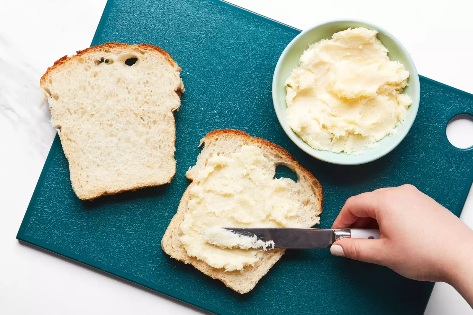 Foto dunha persoa untando marmelada de coco sobre o pan para facer tostadas francesas con rosa cardamomo ruibarbo.