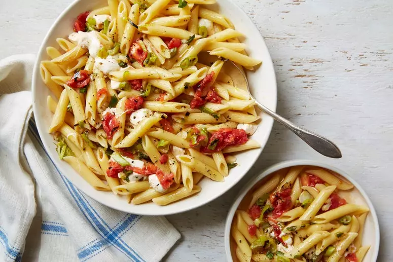 Plater batean eta ontzi batean tomate erretako eta zeriola saltsarekin pastaren argazkia.