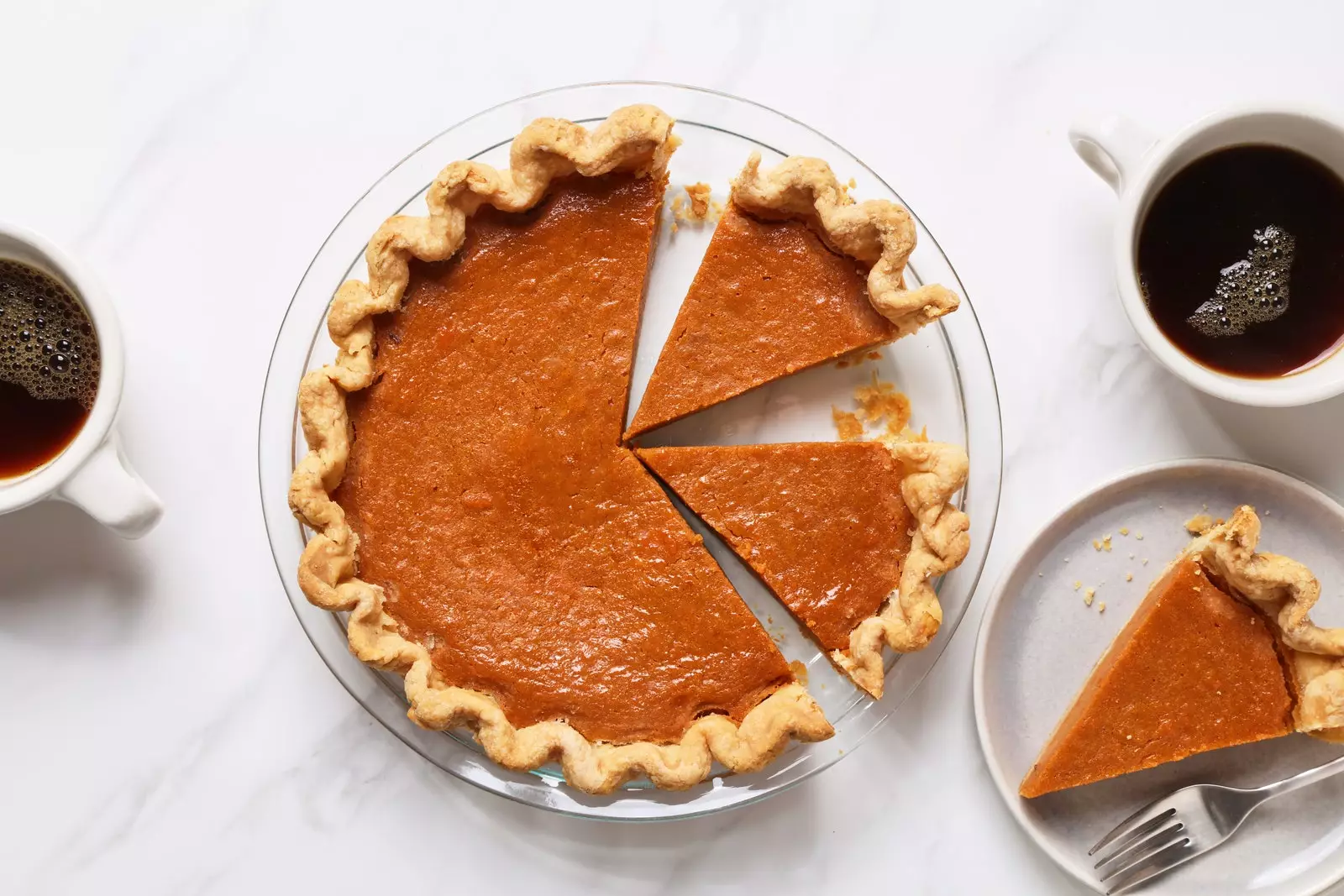 Photo d'une tarte à la patate douce dans un plat à tarte avec trois tranches découpées dont une sur une assiette avec une fourchette à côté...