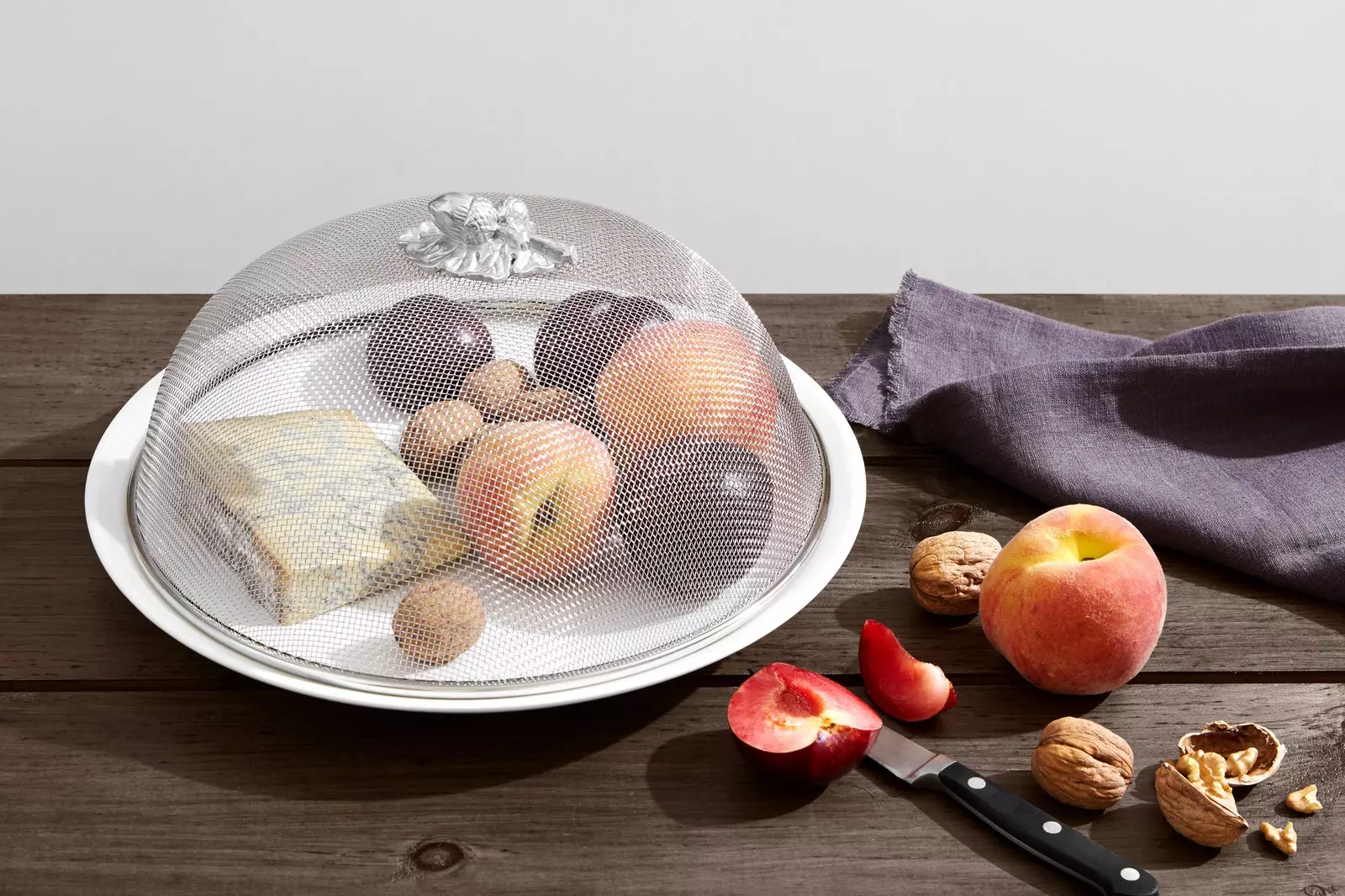 תמונה של קלושה על שולחן עץ עם אפרסקים אגוזי מלך, מפה וסכין.