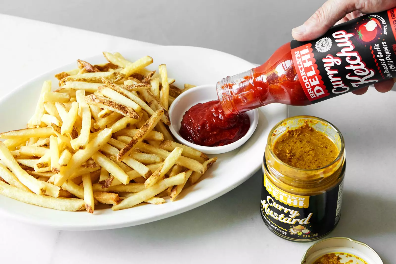 Foto de uma travessa de batatas fritas servida com ketchup e mostarda do Brooklyn Delhi.