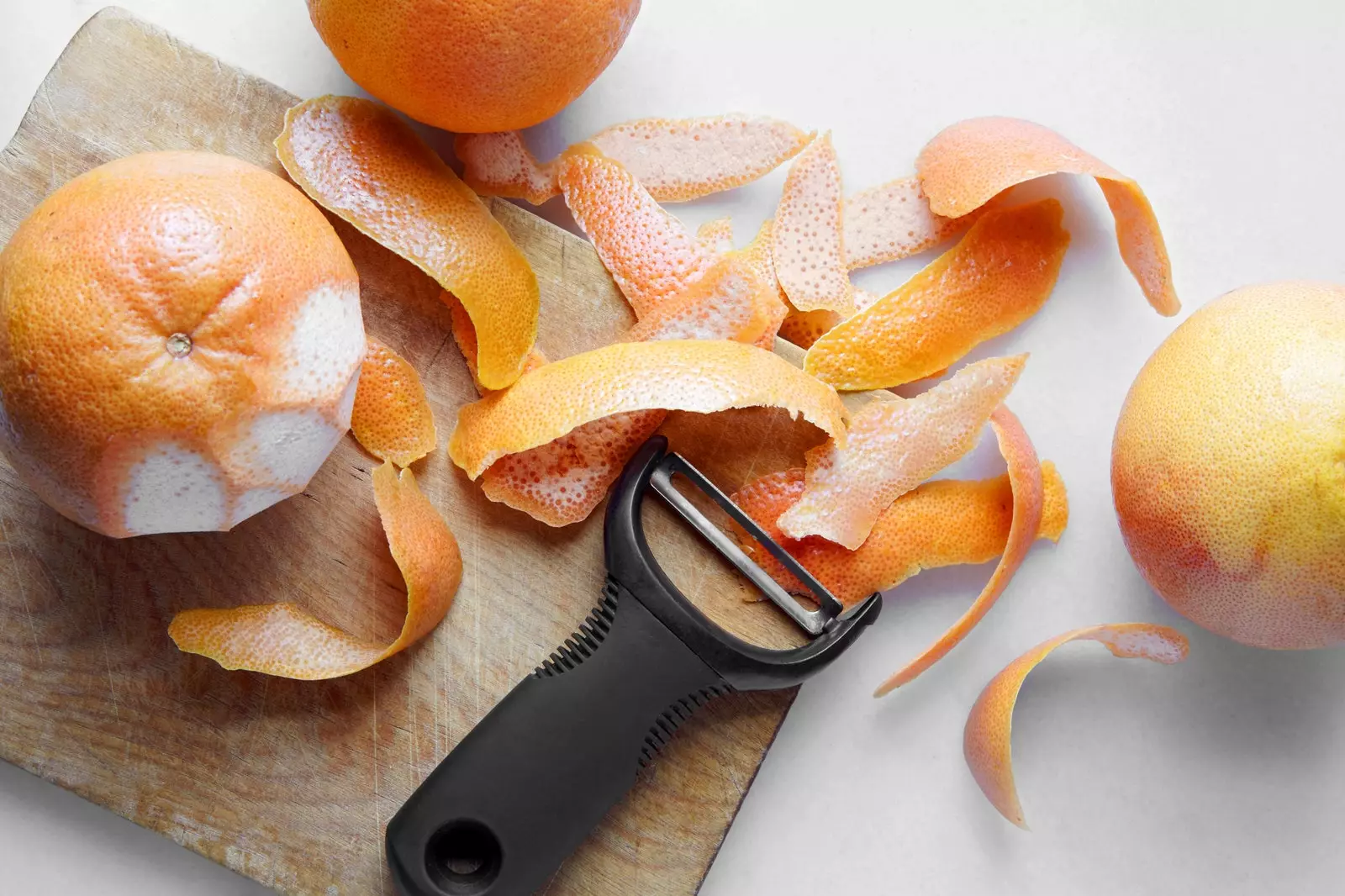 Foto de cascas de toranja em uma tábua de madeira com um descascador e toranja.