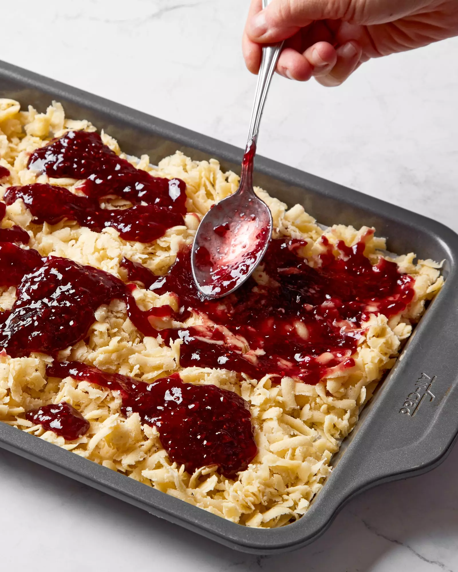 foto di una persona che sparge marmellata di lamponi su pasta biscotto di pane corto