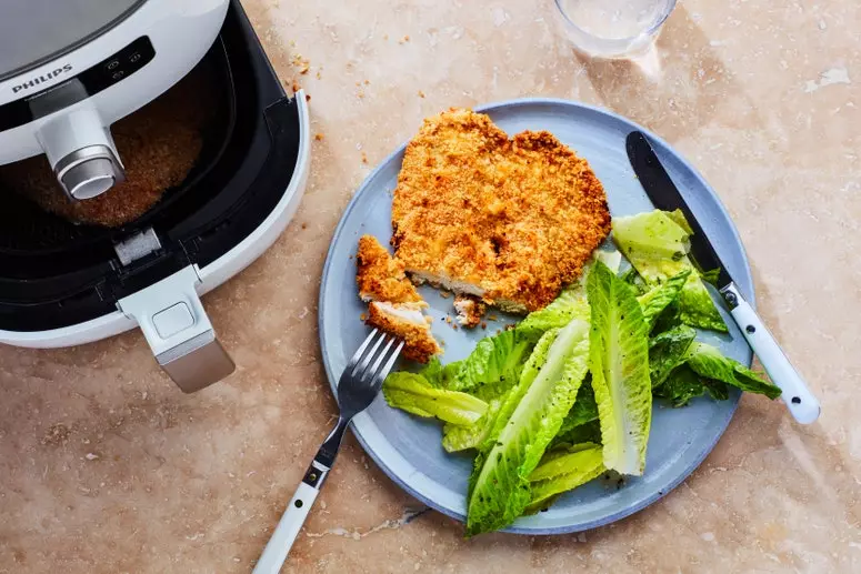 Fénykép a terméktesztünk legjobb légsütőjéről: A Philips Air Fryer. Mellé egy tányér levegőn sült csirkeszelet és saláta. Ez a legjobb légsütő Black Friday ajánlat 2020-ban.