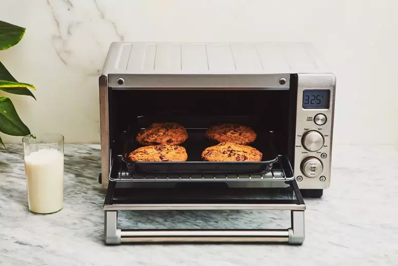 Une photo de notre choix pour le meilleur four grille-pain, le Breville Smart Oven, avec des biscuits aux pépites de chocolat qui cuisent à l'intérieur et un verre de lait sur le comptoir à côté.