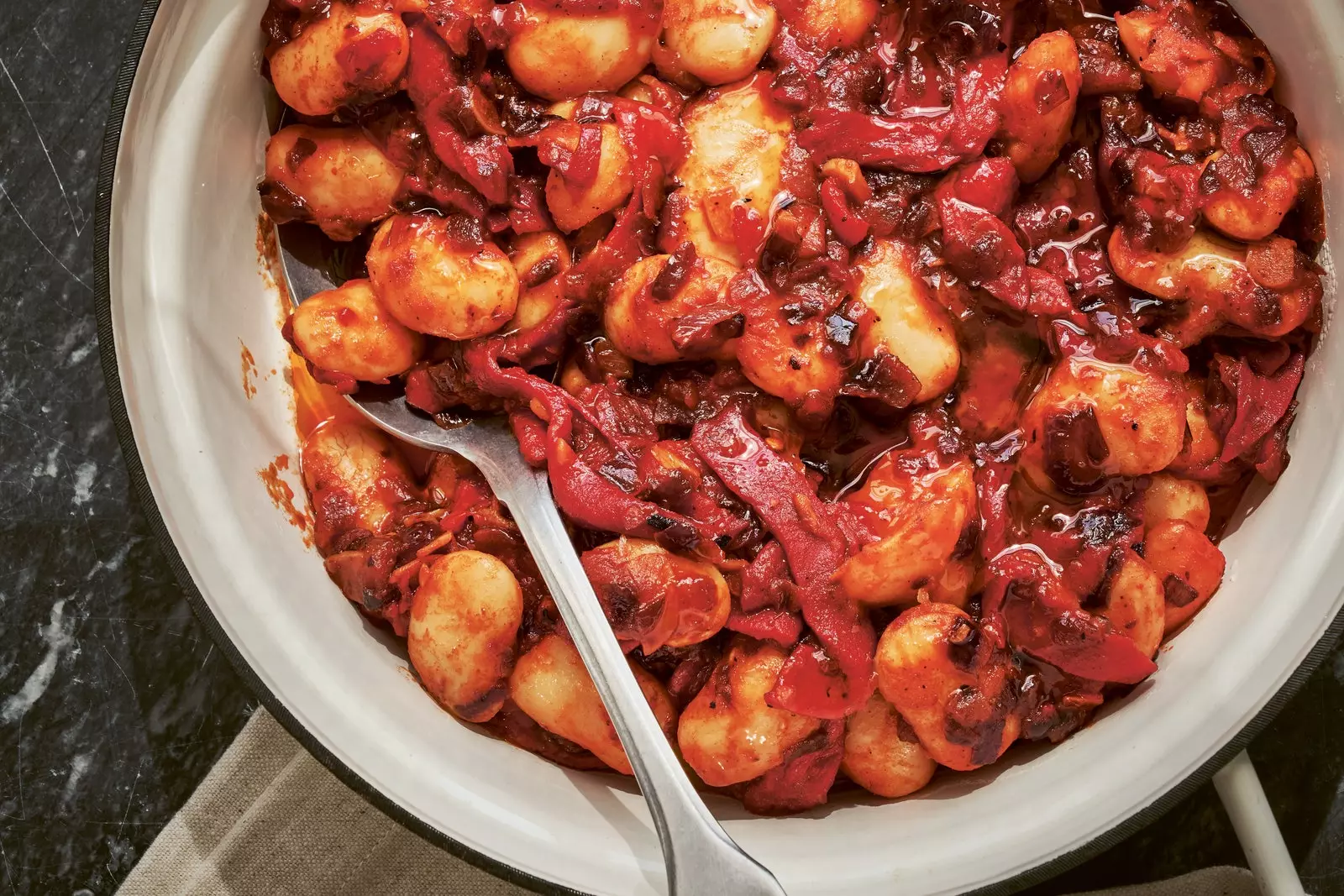 Boterbonen met piquillo-pepers in een witte kookpot met een lepel.