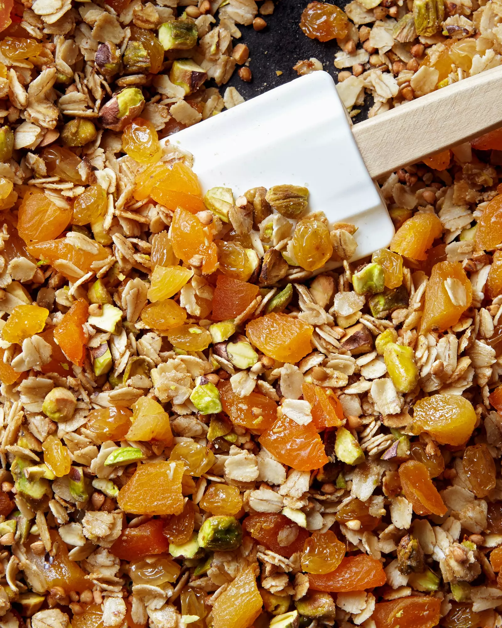 Foto av havre, aprikos, pistasjnøtter og quinoa som blandes med en gummispatel.
